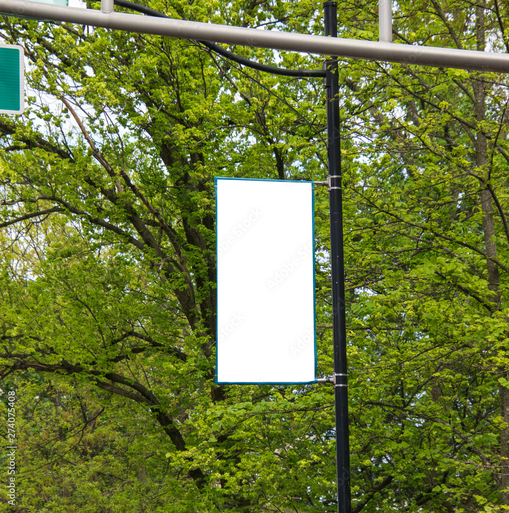 Blank white sign attached to a light pole with trees in the background ...
