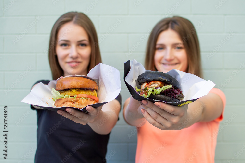 young beautiful girls students stand near the blue wall, hold burgers ...