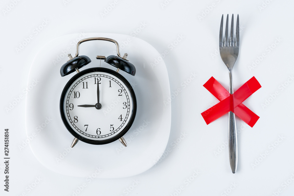 Black alarm clock in white plate with fork on the table. Time to eat ...