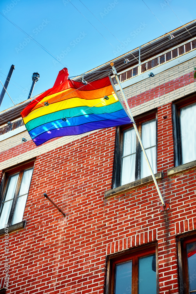 Rainbow gay pride flag waving on the flag pole of a brick building ...