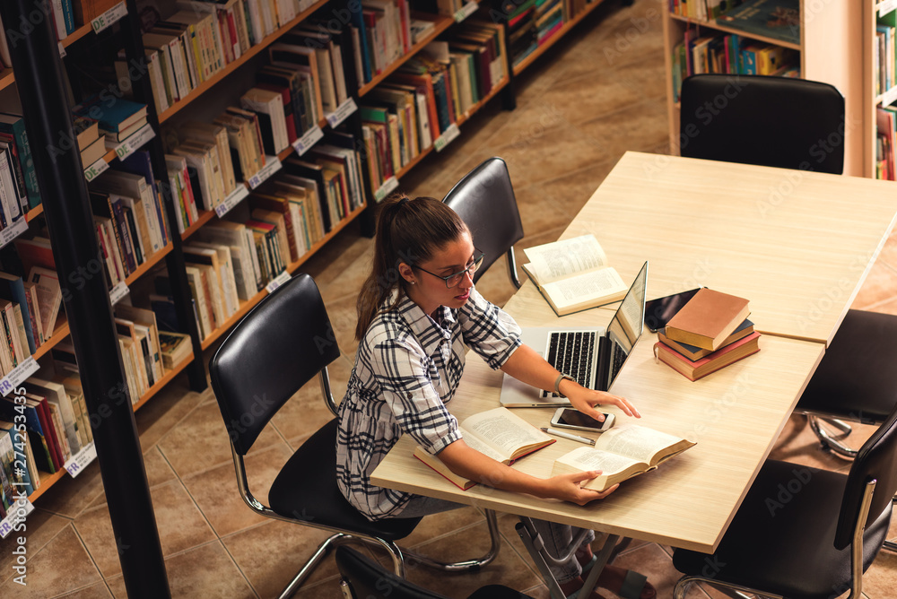 Young female student study in the library using laptop for researching ...