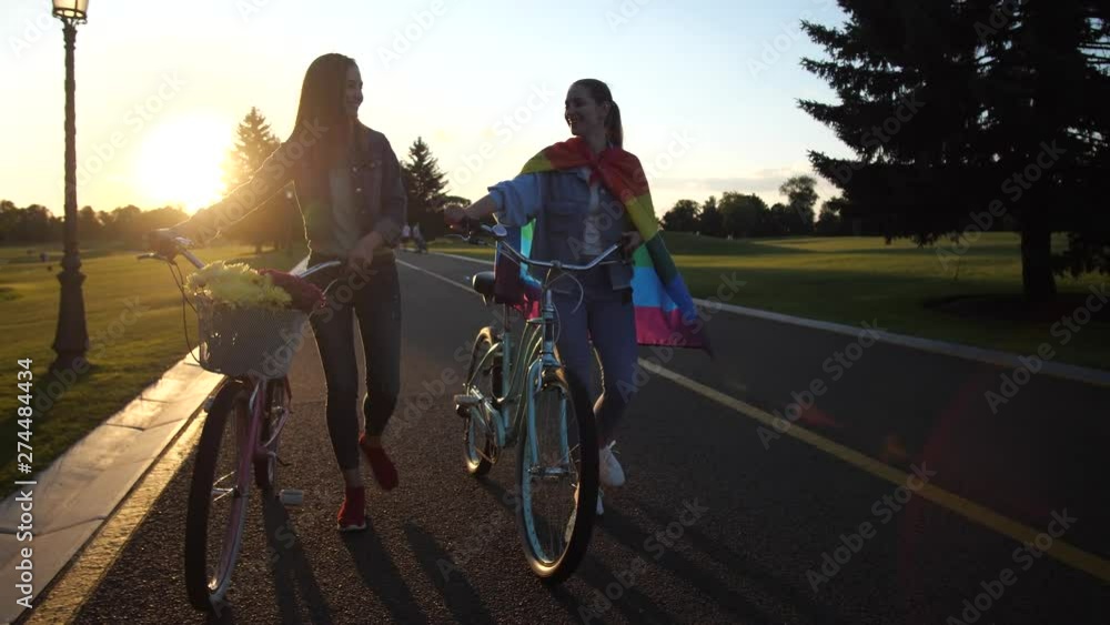 Attractive Lesbian Couple Relaxing During Walk In Park Taking Bikes