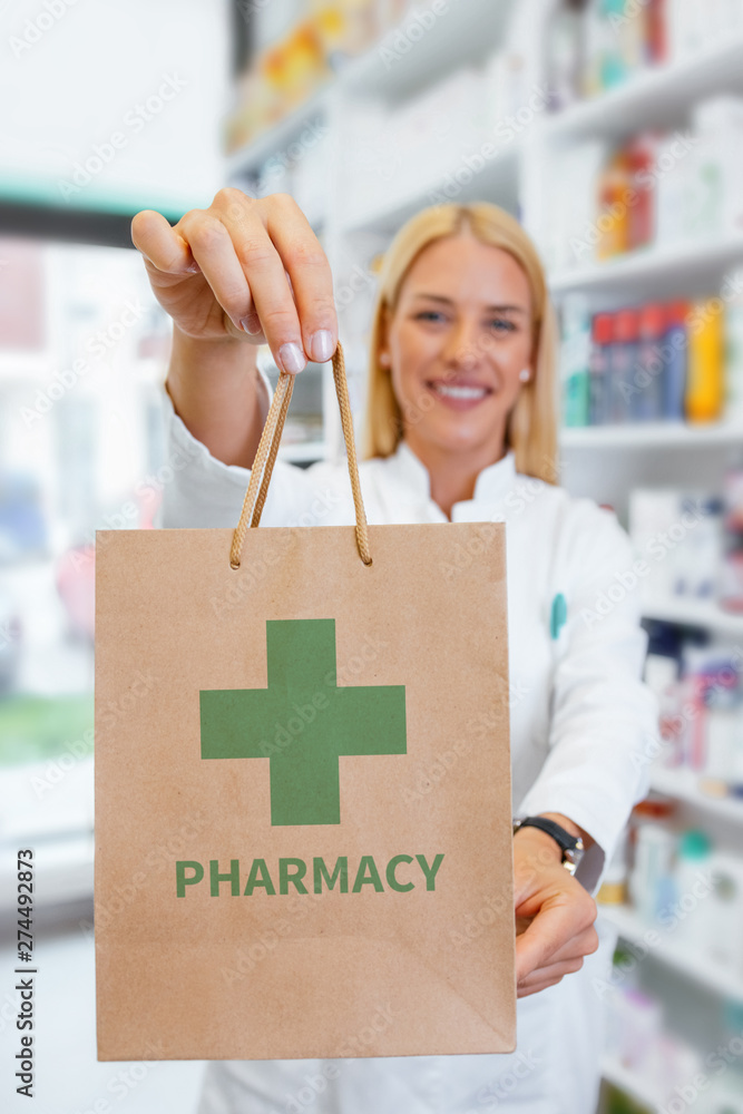 Pharmacist holding paper bag with a green Pharmacy logo in a drugstore ...