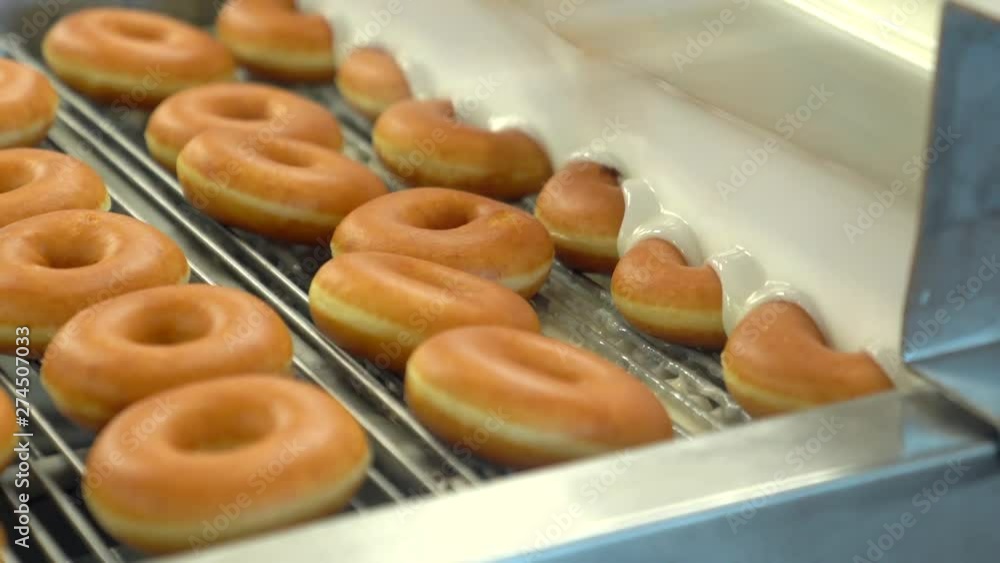 This video shows a busy donut factory adding icing to hot, fresh glazed ...