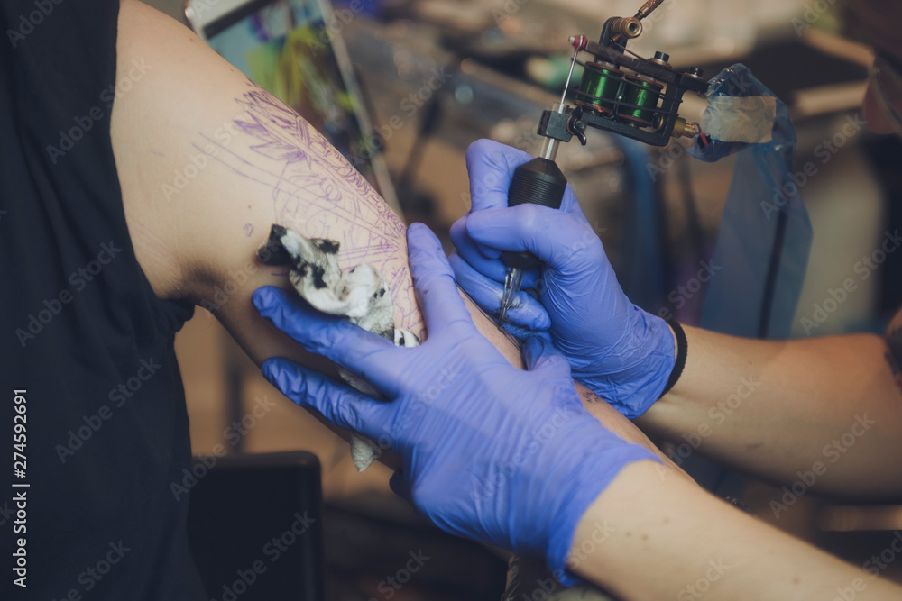 Detail of a professional woman tattooer tattooing the arm of a young ...