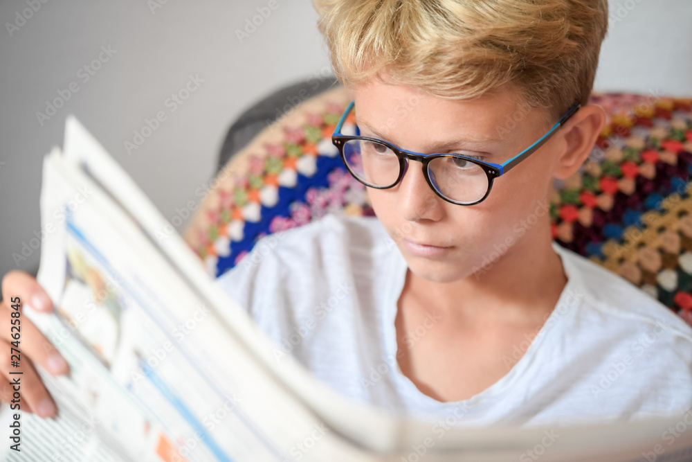 Beautiful young boy reading a newspaper at home. Blonde child reads ...
