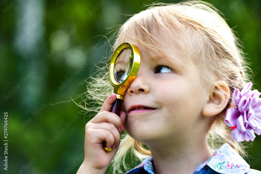 The child looks through a magnifier. Beautiful little girl looking ...