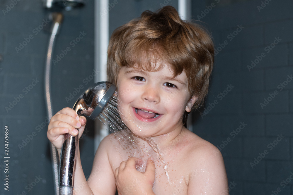 Smiling beautiful boy bathing under a shower at home. Cute 5 year old child bathes in a shower ...