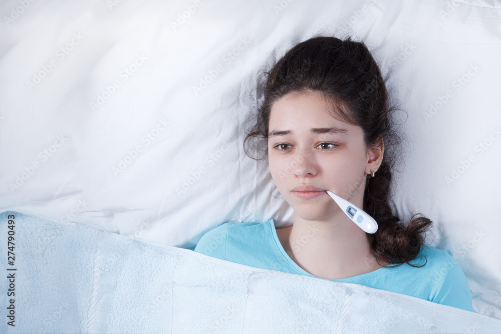 The sick girl the teenager with the thermometer in a mouth, on a bed ...