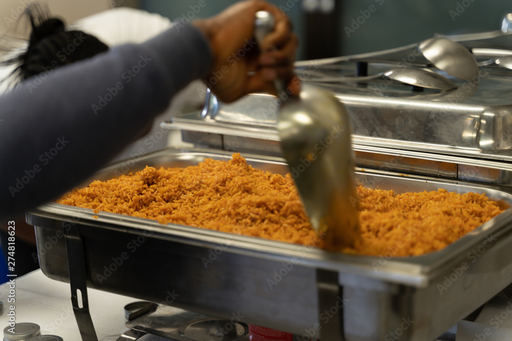 Nigerian African American Woman filling chaffing Dish with jollof rice ...