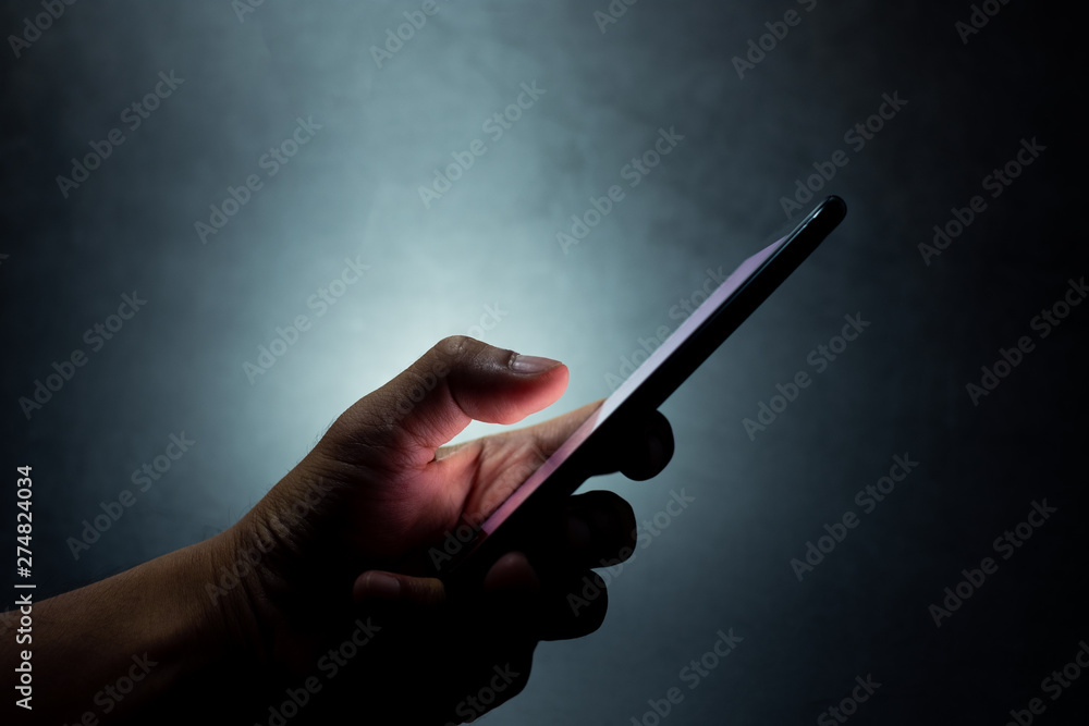 silhouette hand holding and touching a mobile phone screen in the dark ...