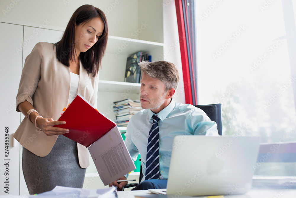 Two business people looking a red file in a small office in a real life ...