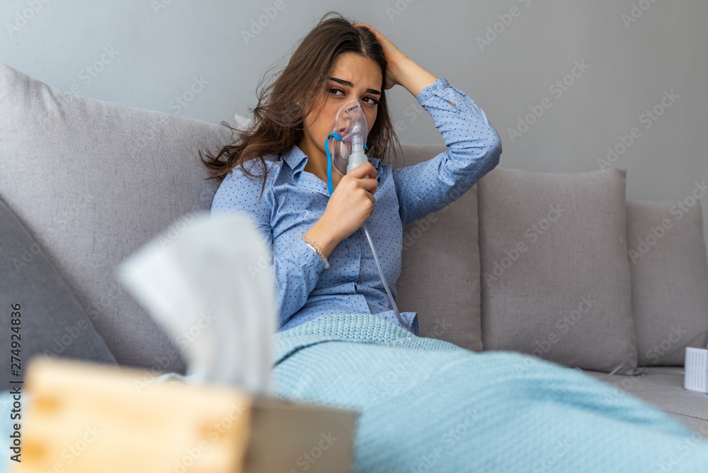 Portrait of a young woman doing inhalation at home. Use nebulizer and ...