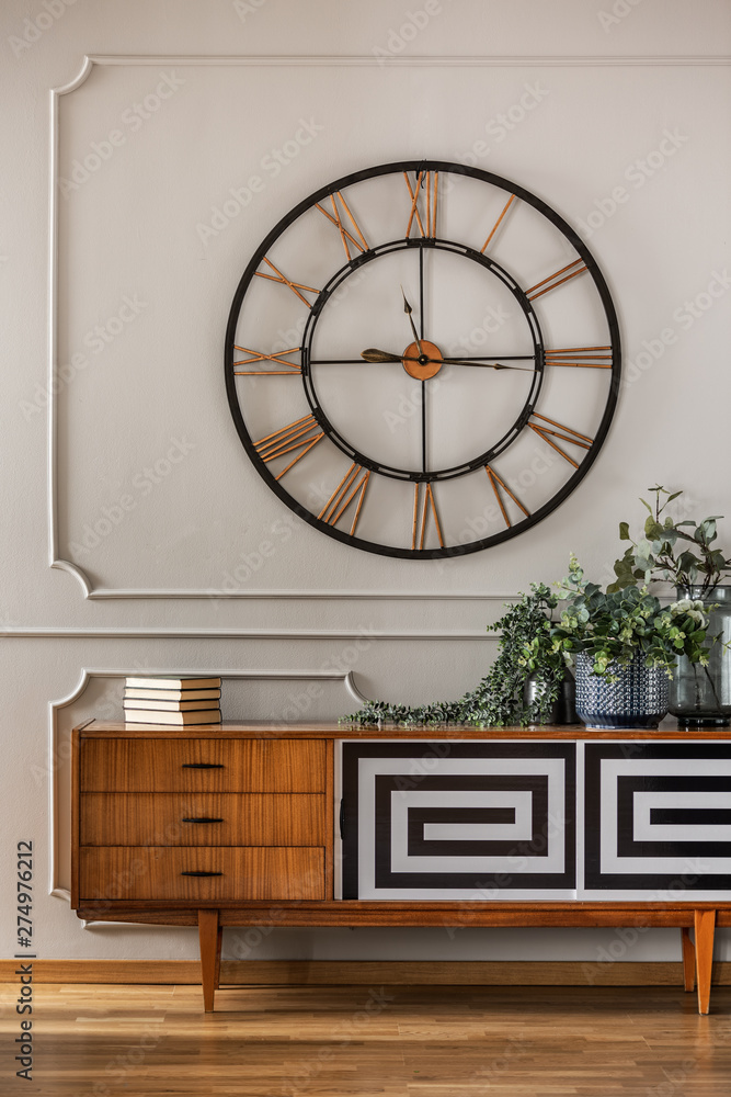 Real photo of a large, metal clock hanging on a white wall with molding ...