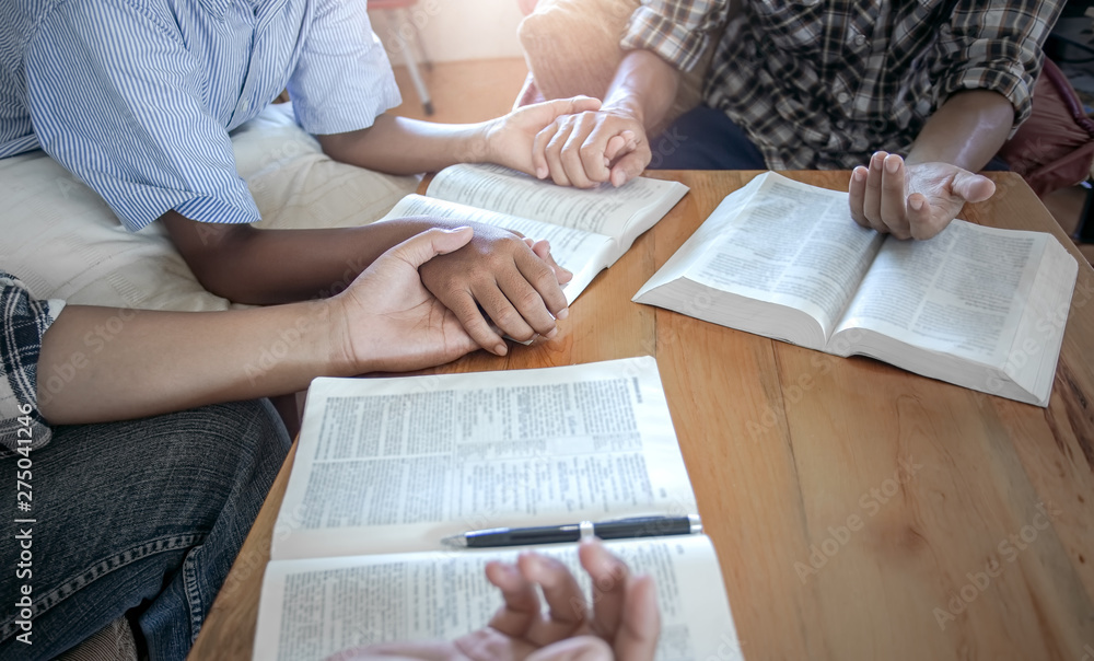 Christian group praying together around wooden table with open bible in ...