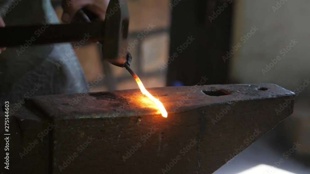 Blacksmith striking a molten iron rose with a hammer on an anvil in a ...