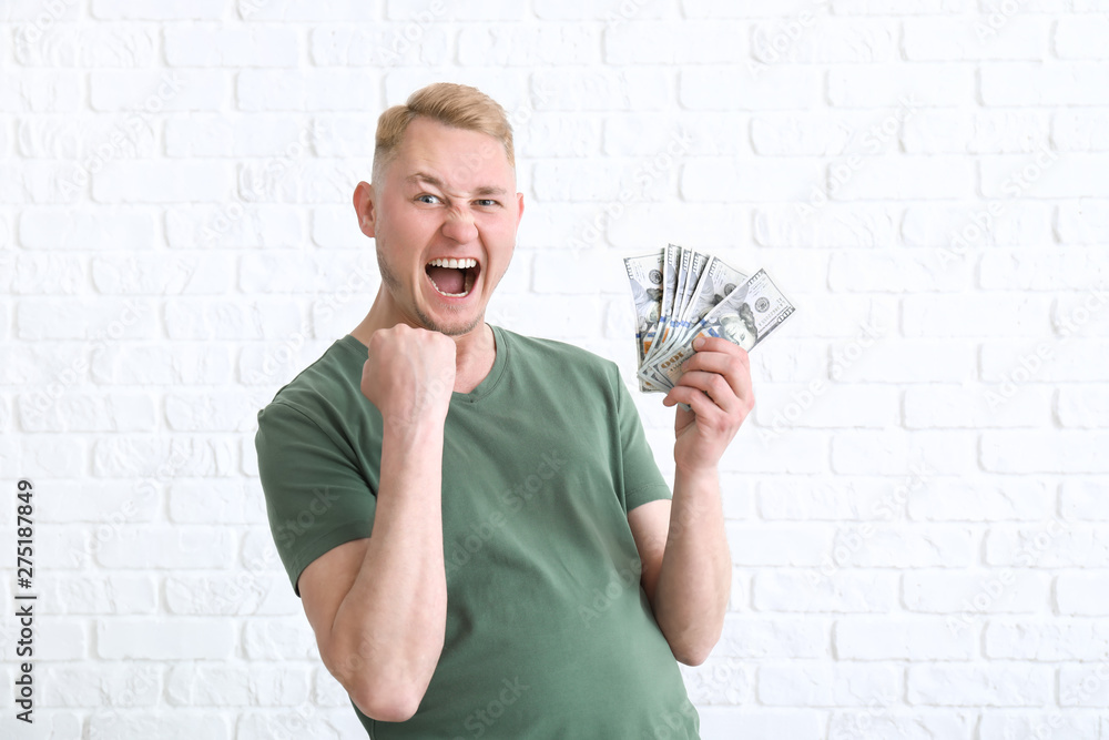 Happy young man with dollar banknotes on white brick background Stock ...