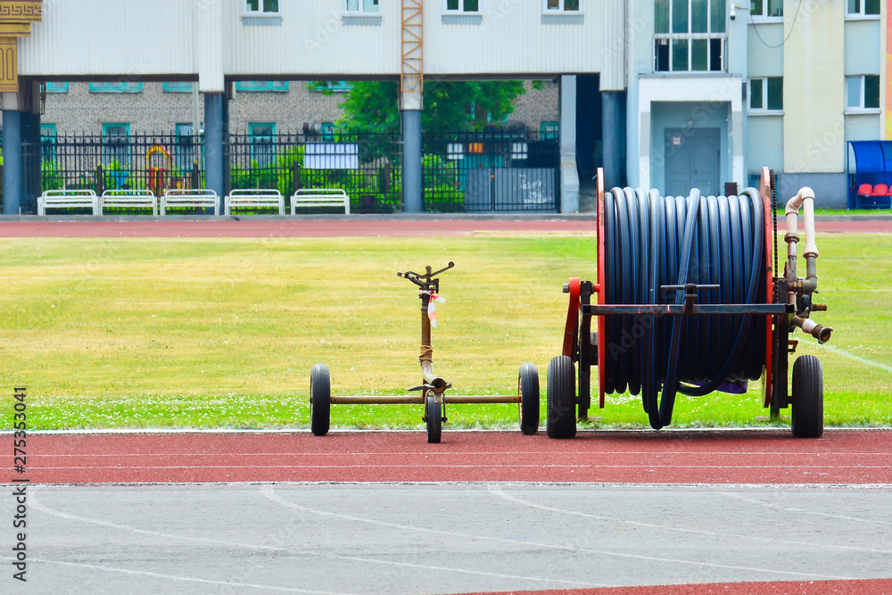 Mobile sprinkler on an empty green soccer field. Big drum with a hose ...