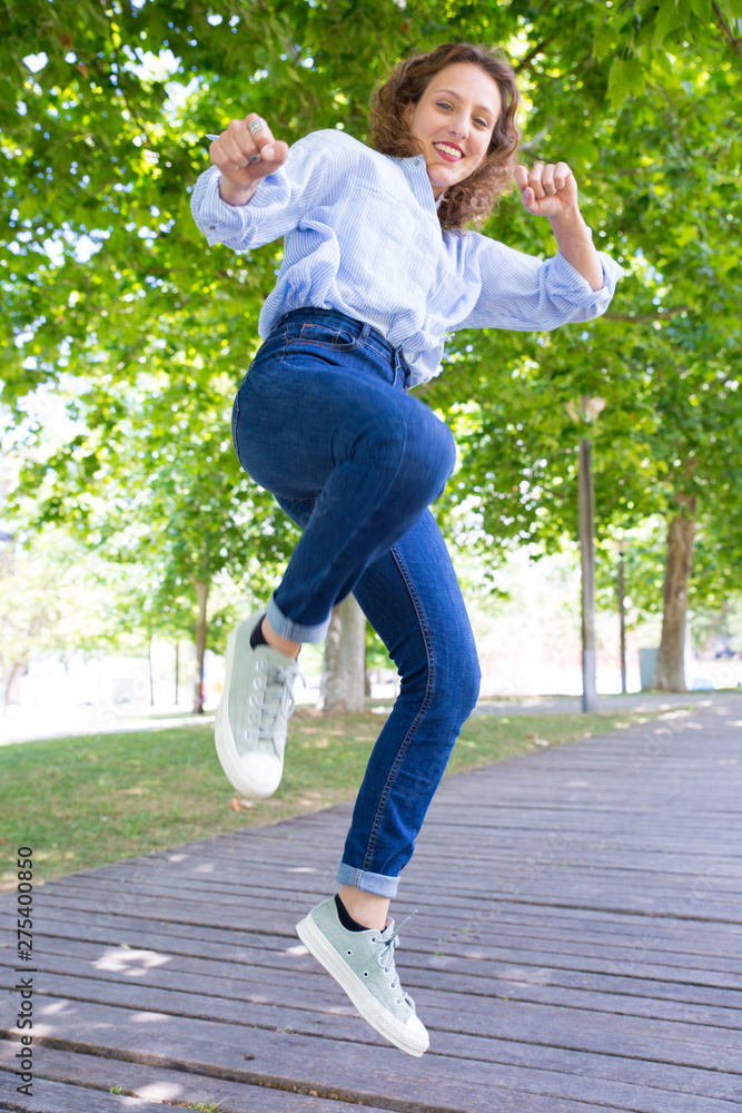 Joyful excited girl having fun outdoors and jumping as kickboxer or ...