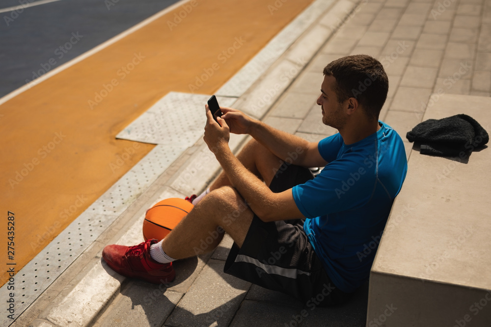 Basketball player using mobile phone while relaxing on basketball court ...