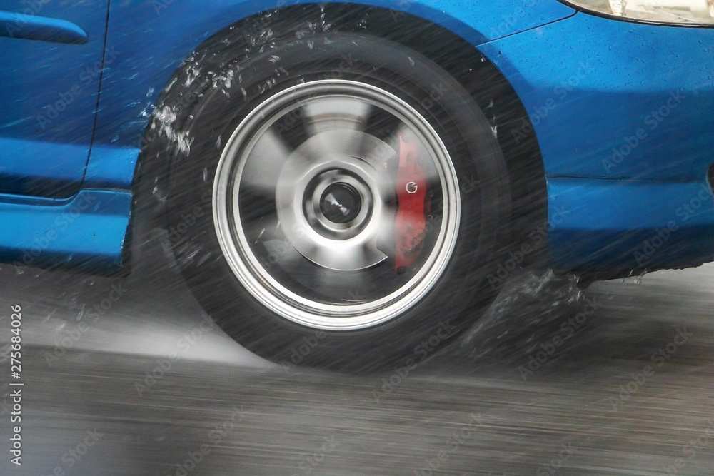 Detail of the rear wheel of a car driving in the rain on a wet road ...