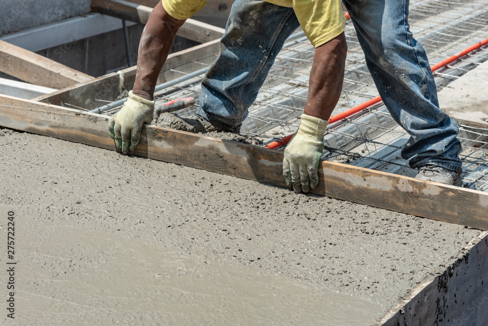 Worker levels a floor cement mortar. Using a straight wooden board to ...
