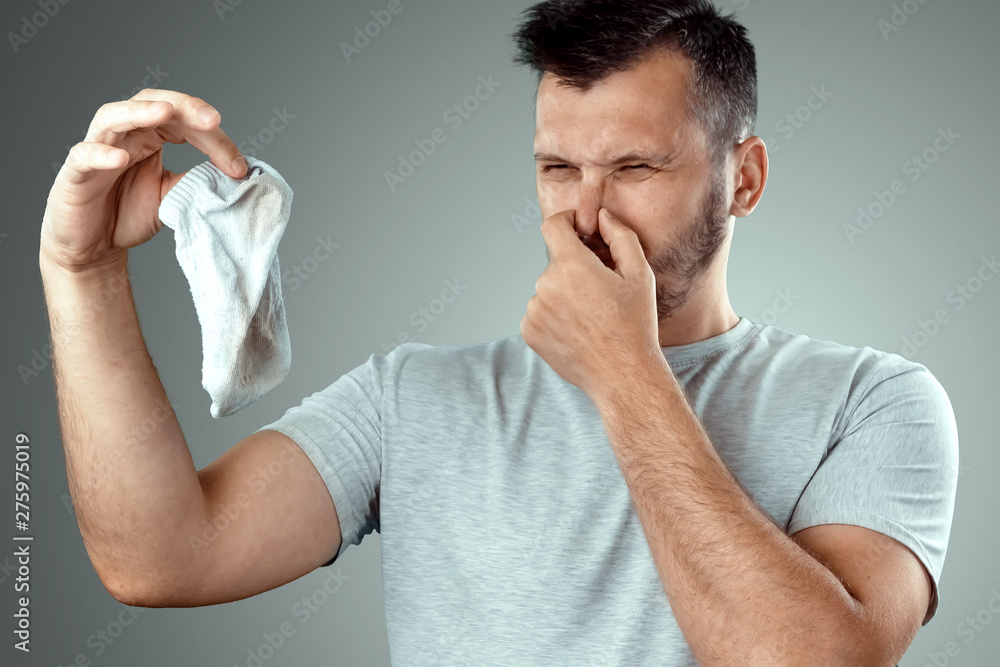 A young man holds his smelly socks and covers his nose with his hand ...