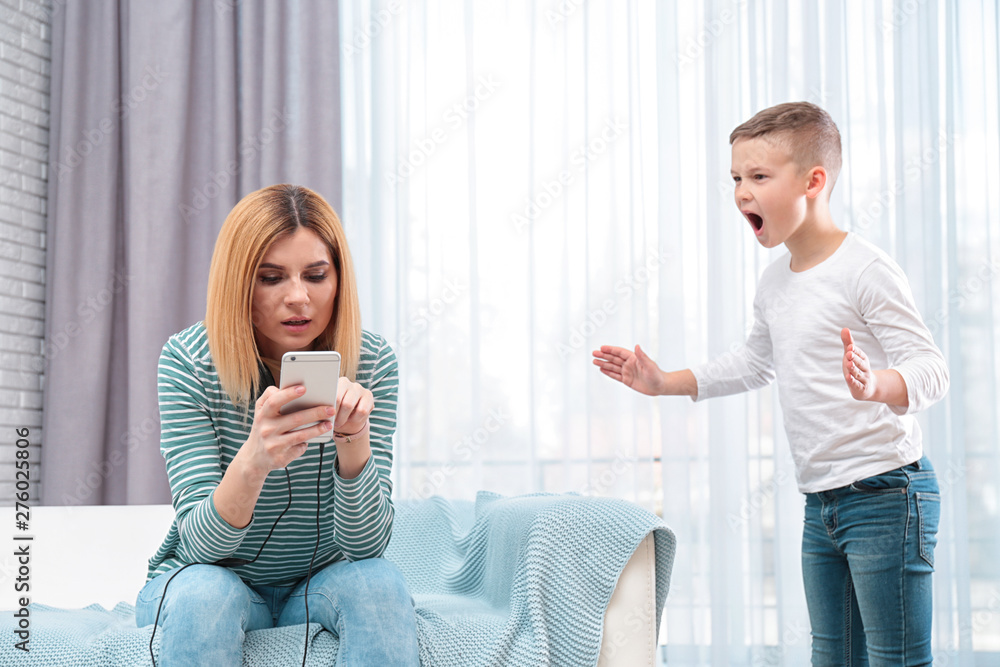 Mother using mobile phone while her son screaming and asking for ...