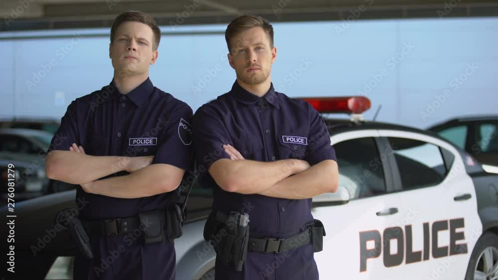 Brave male officers with hands crossed standing against police car on ...