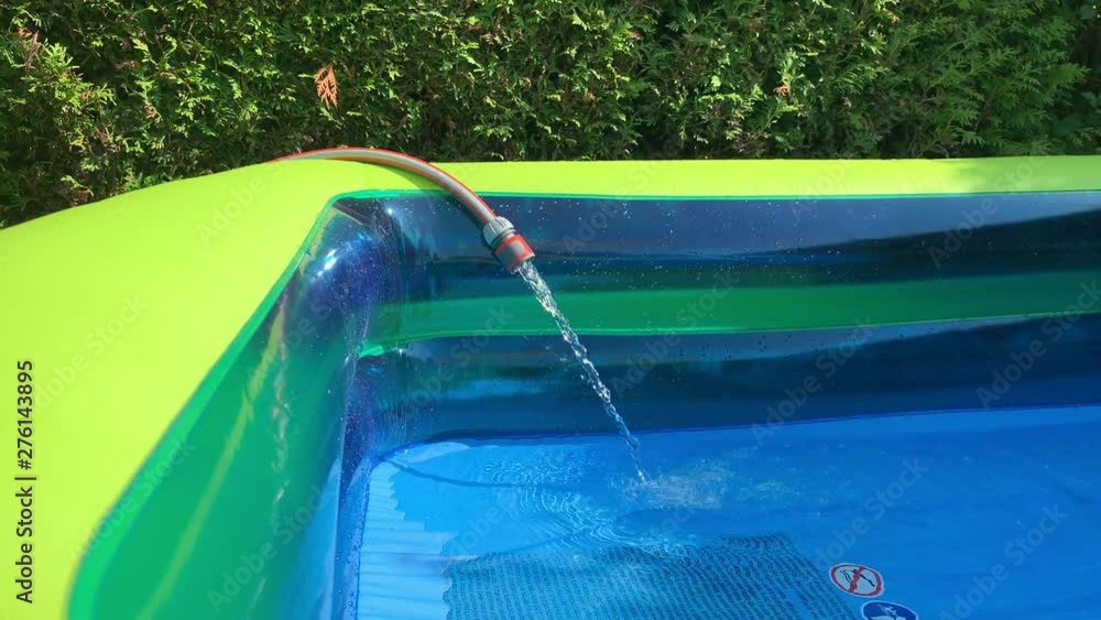 [Static, side view] Hose lying over pool corner, filling outdoor pool ...