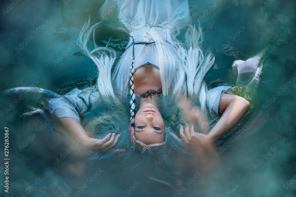A girl elf in a white dress is floating in the water. Model in a ...