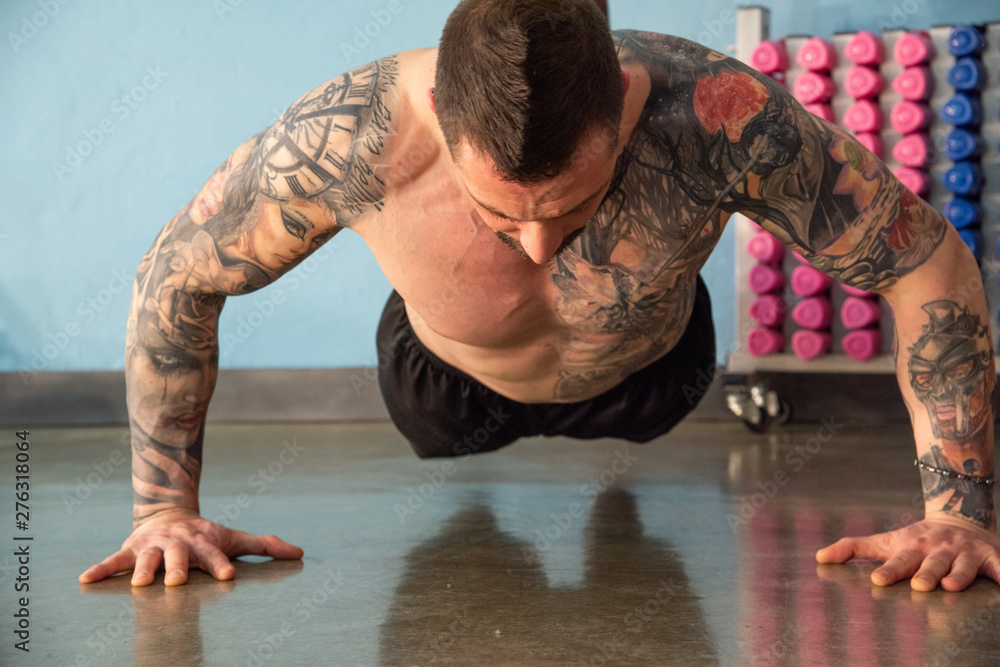Personal trainer with tattoos performs exercises with his arms raised ...