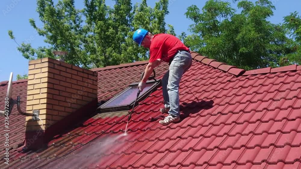 House roof cleaning with water pressure tool. Worker on top of building ...