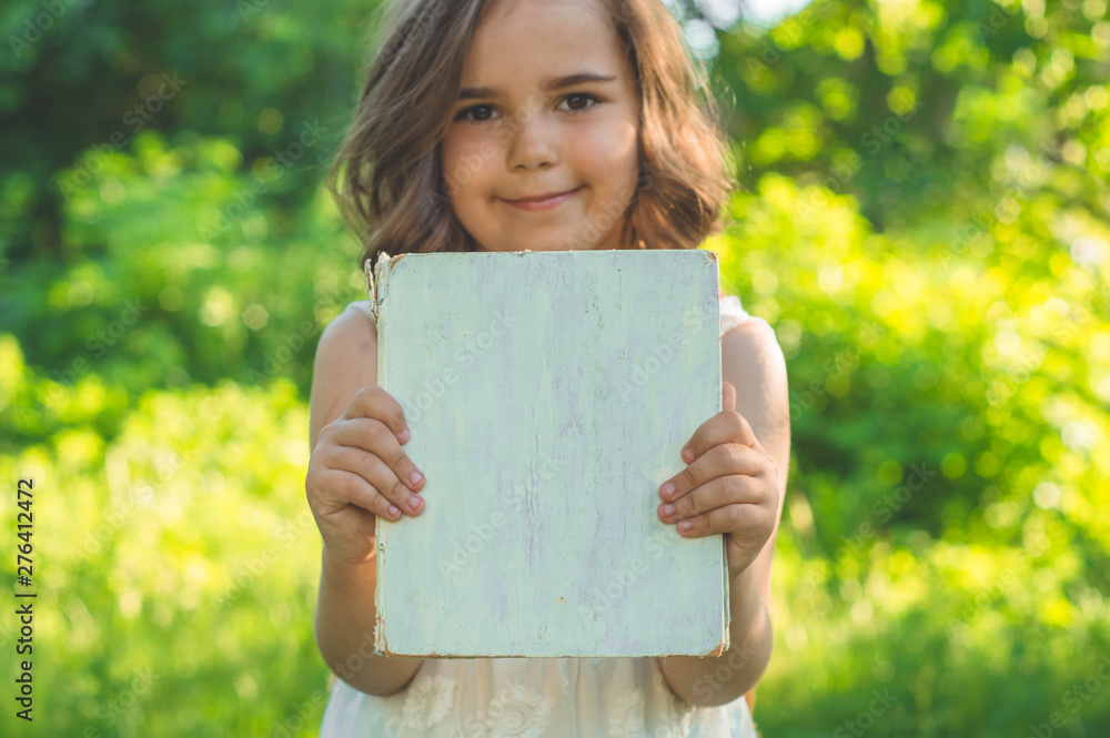 Cute industrious child is standing with a book and a briefcase outdoors ...