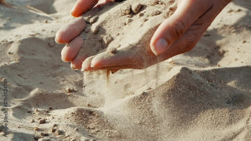 SLOW MOTION, CLOSE UP: The sand passes through the fingers of a young ...