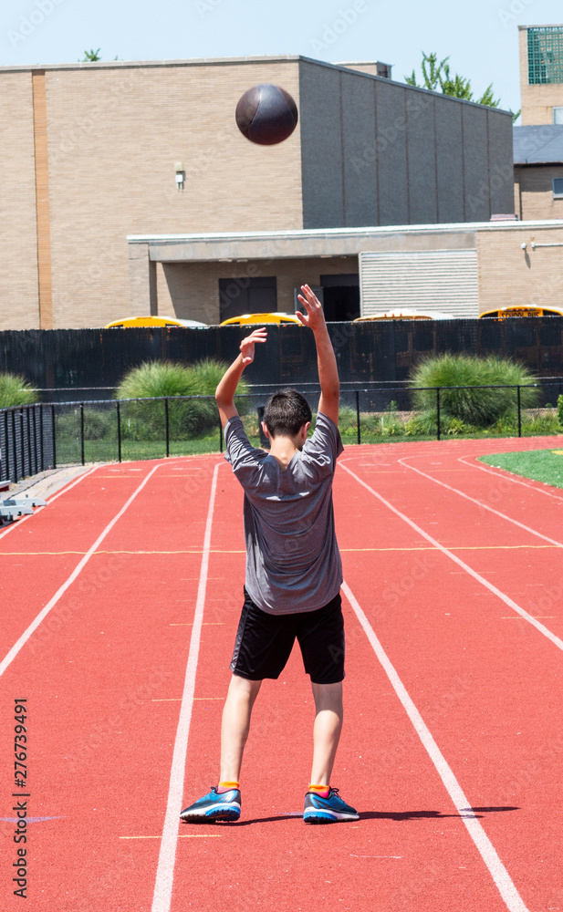 Teenage boy throwing a medicine ball backwards over his head onn a ...