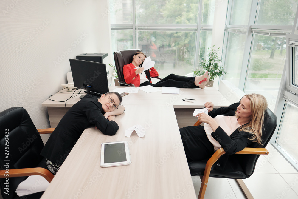 Three beautiful young girls in business suits are sitting at the office ...