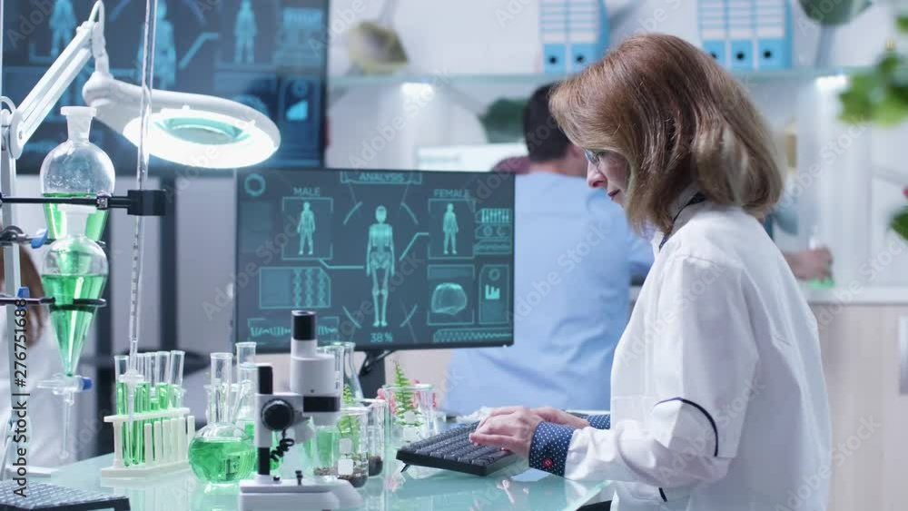 Adult biologist workign in modern laboratory. She is typing on computer ...