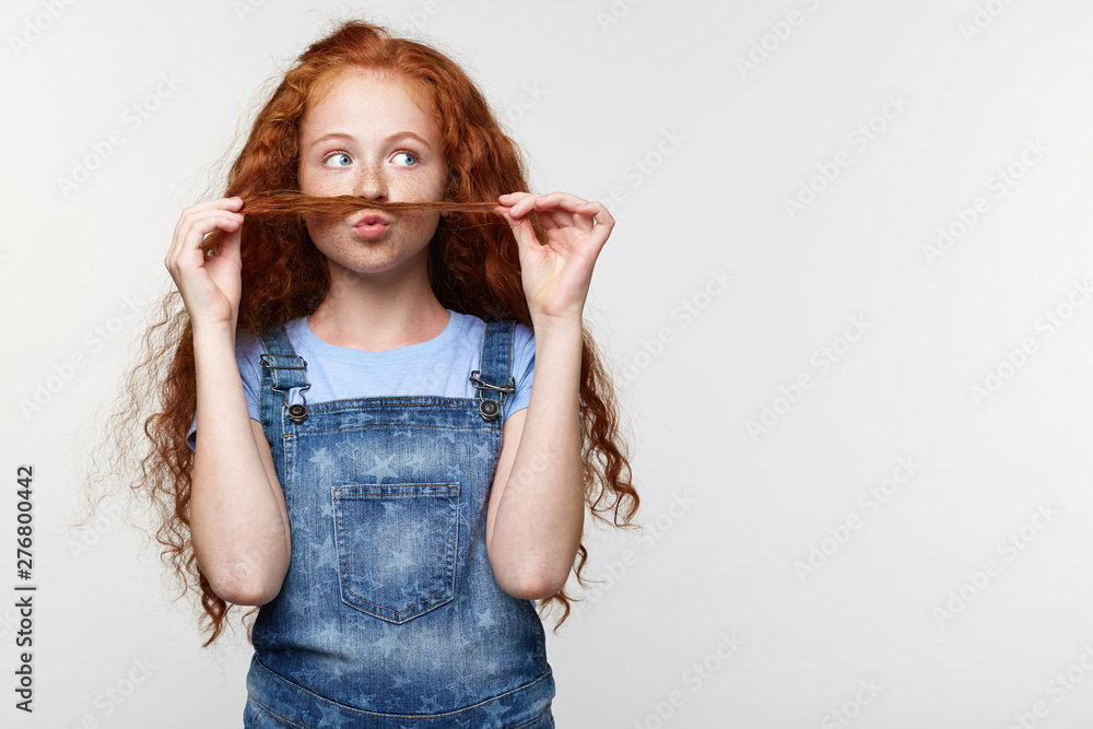 Joyful cute little girl with ginger hair and freckles, looks away ...
