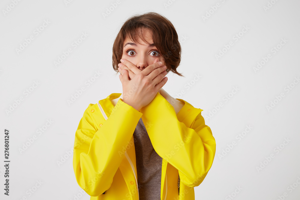 Portrait of scared short-haired curly woman in yellow rain coat, heard ...