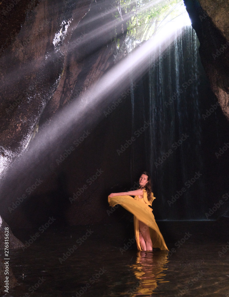 Famous Bali waterfall in the cave Tukad Cepung. Young girl in yellow ...