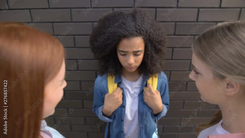 Female teenagers looking at younger black schoolmate, bullying problem ...