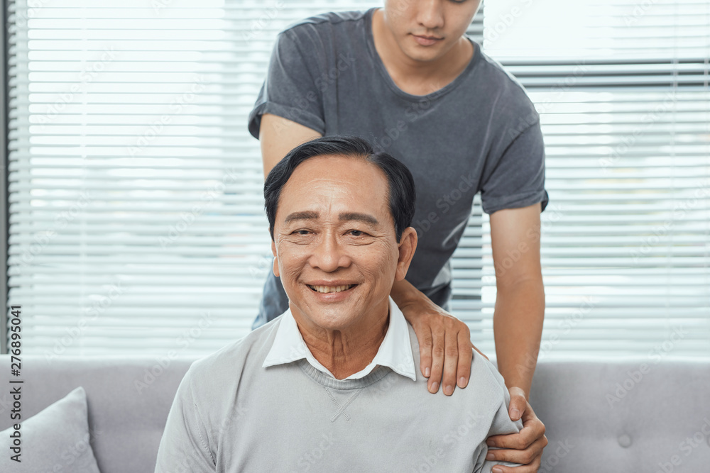 Asian old man shoulder pain, sitting on sofa , son massaging father ...