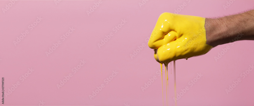 man's hand clenched into a fist smeared in yellow paint on a pink color ...