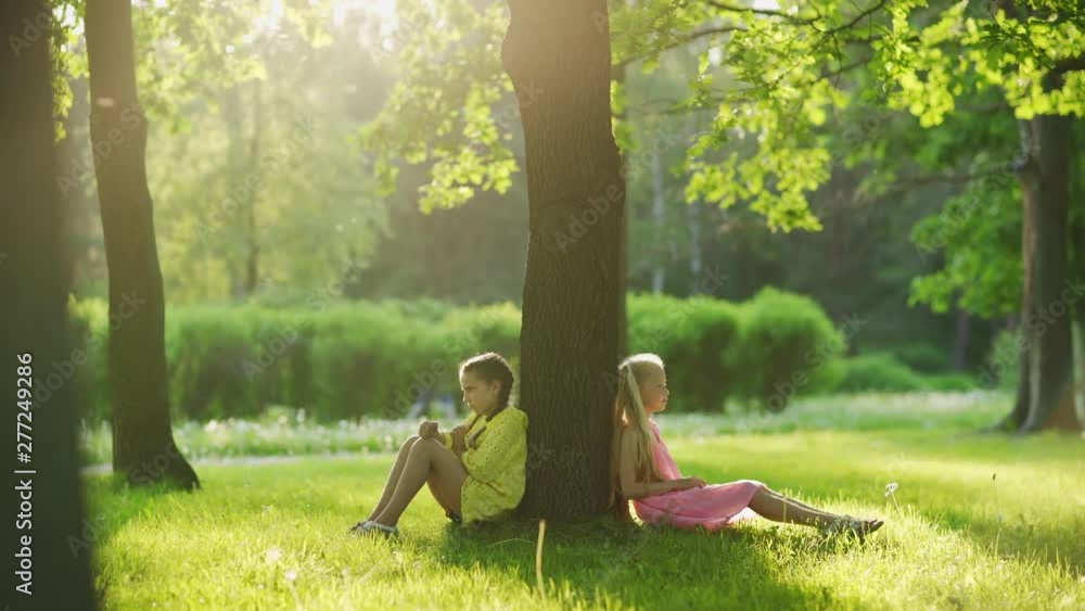 Tracking right shot of two unhappy little girls sitting on grass in ...
