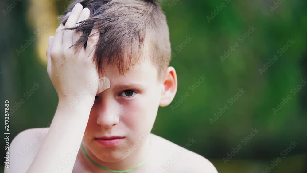 Unhappy boy with closed wound on face outdoors. Young teenager has a ...