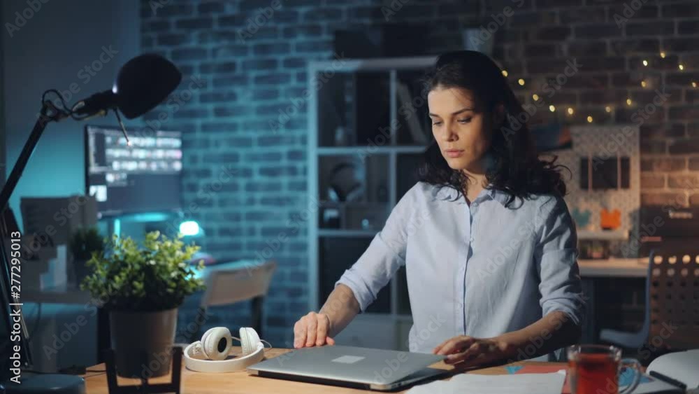 Girl office worker is leaving workplace at night turning off laptop and ...