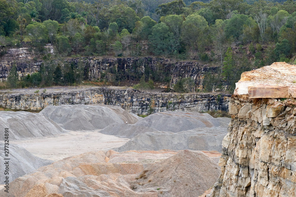 The rock-faces and piles of gravel, of a large working quarry pit, with ...