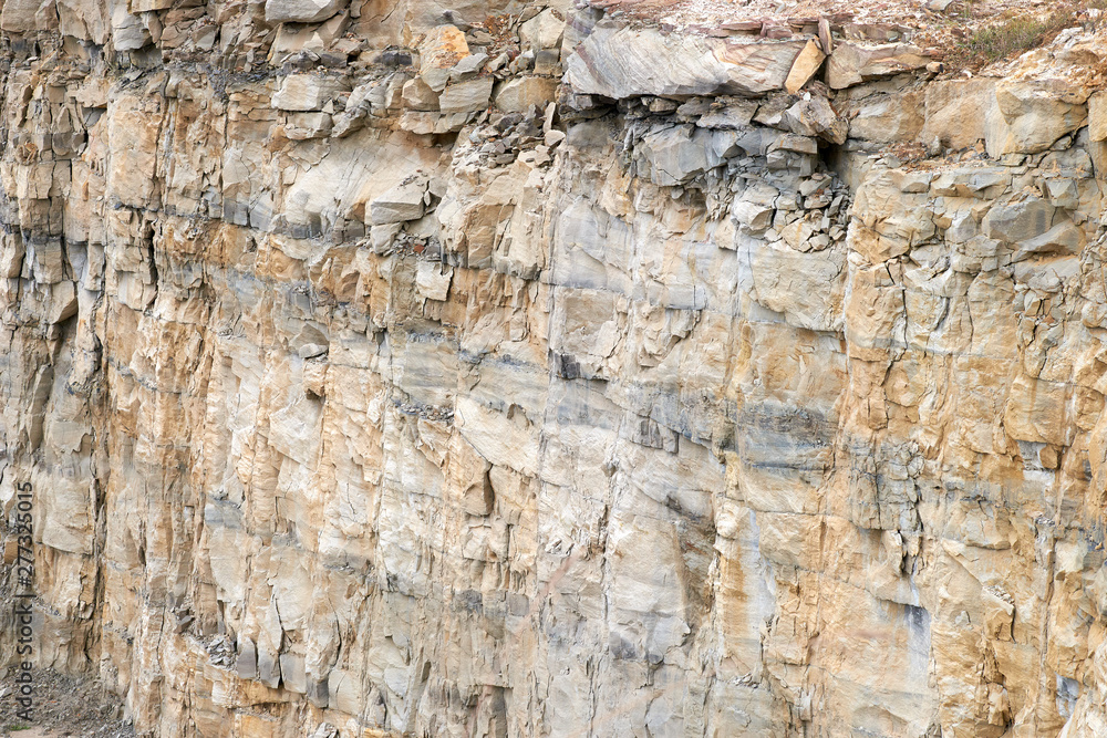 The rough-hewn vertical rock-face of a large working gravel quarry pit ...