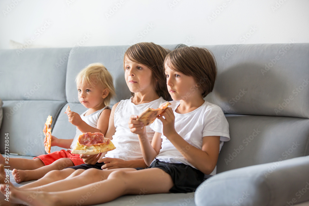 Cute children, sitting on couch, eating pizza and watching TV. Hungry ...